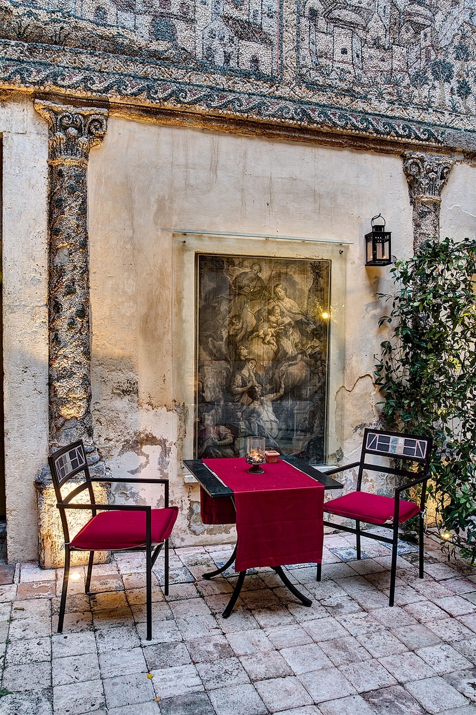 Uma área externa com mesa e cadeiras, um mural na parede e um candeeiro.