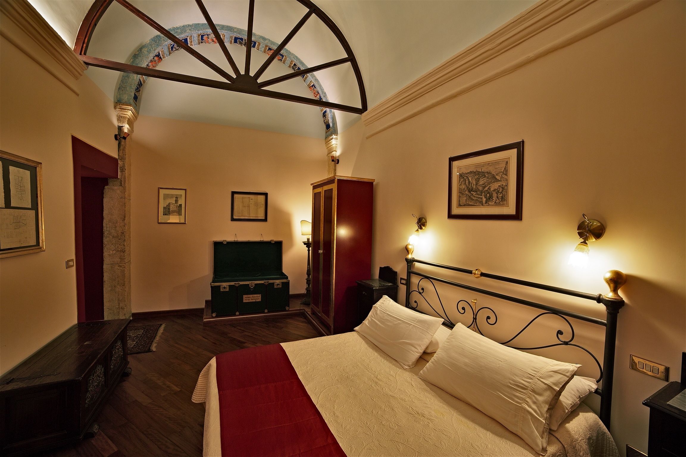 Quarto de hotel com uma cama, uma cômoda verde, um banco de madeira e um teto grande em arco.