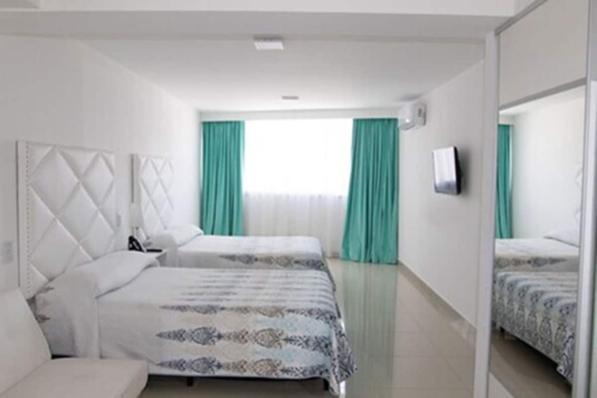 Quarto de hotel com duas camas, um espelho grande e uma janela com cortinas.