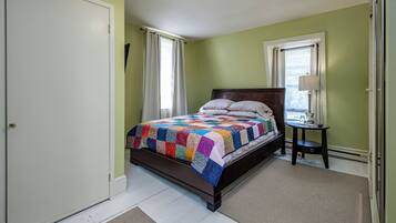 Um quarto com uma cama, mesa de cabeceira, abajur e uma porta.