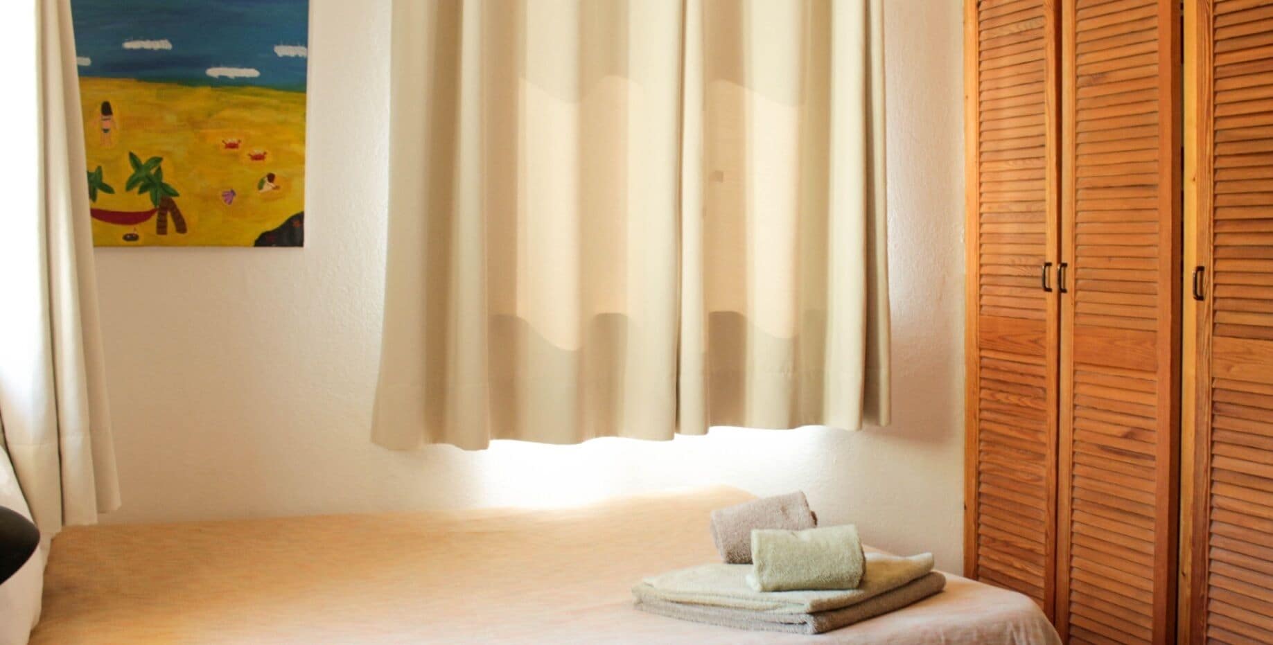 Quarto com cama, um quadro, janela com persianas e portas de guarda-roupa de madeira.