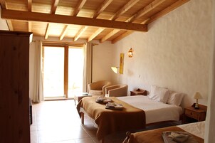 Quarto de hotel com uma cama, uma cadeira, uma escrivaninha e uma luminária.