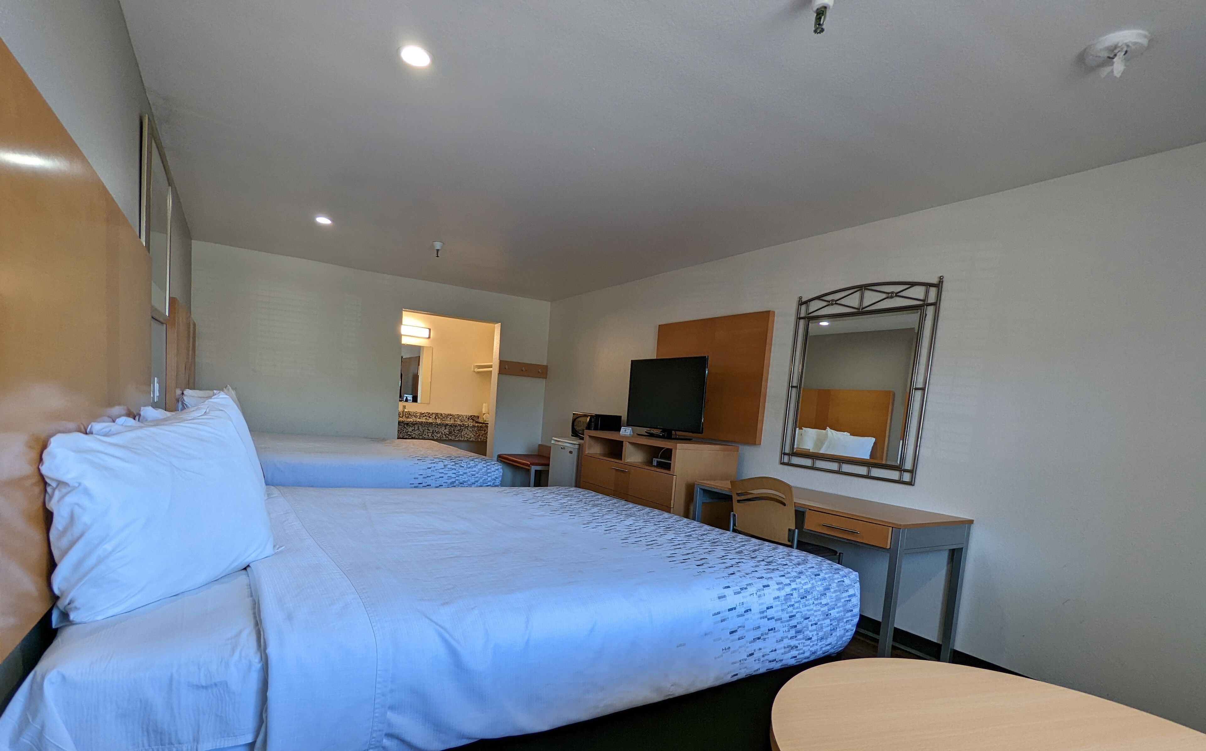 Quarto de hotel com duas camas, uma escrivaninha, uma televisão e um espelho.