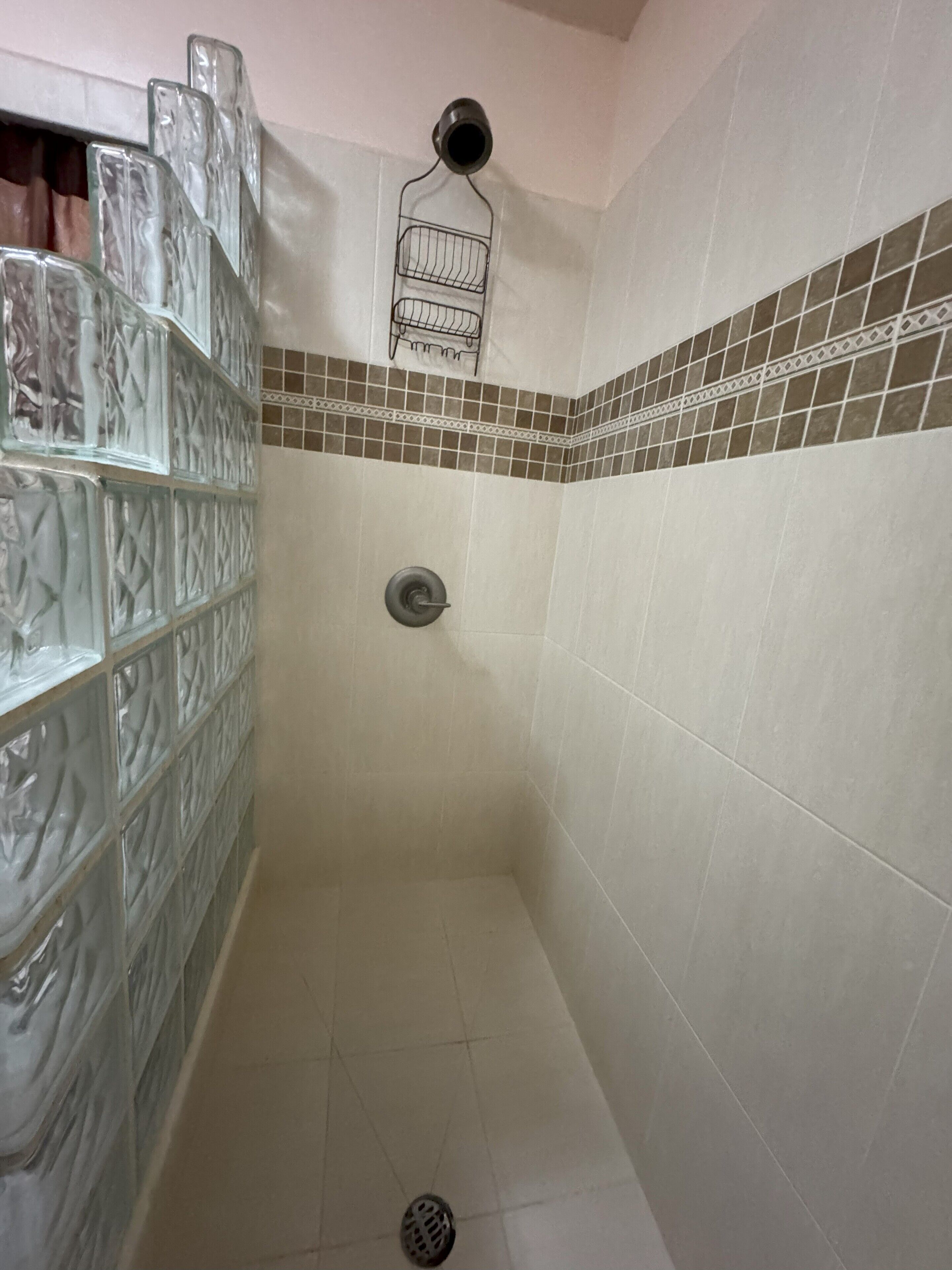 Área de chuveiro com paredes azulejadas, box de vidro e porta-toalhas.