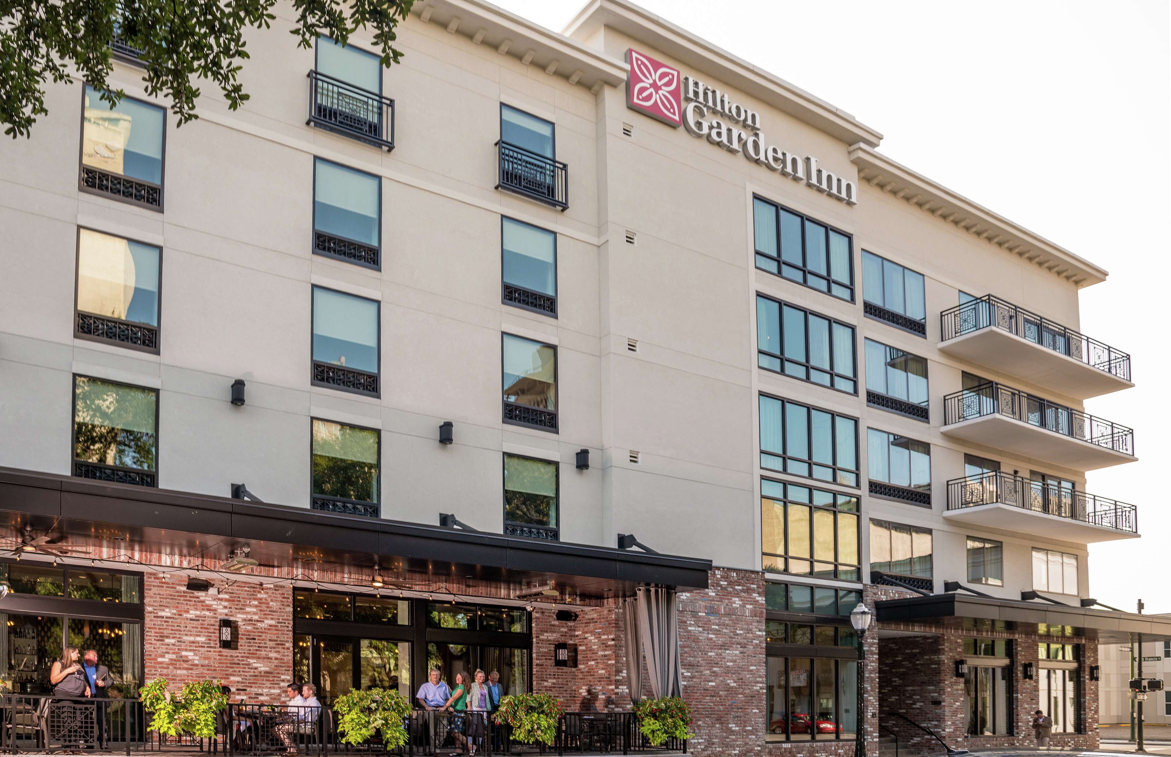 Um hotel Hilton Garden Inn com fachada de tijolos, área de estar ao ar livre e várias varandas.