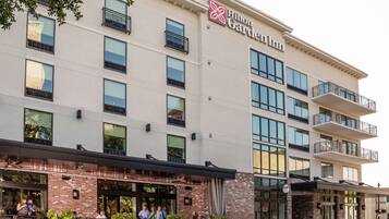 Um hotel Hilton Garden Inn com fachada de tijolos, área de estar ao ar livre e várias varandas.