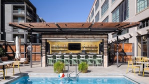 Um bar no terraço com piscina, mesas ao ar livre e área de bar com uma tela de televisão.