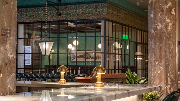 Uma área de bar com bancada de mármore, banquetes estofados verdes e iluminação pendente.