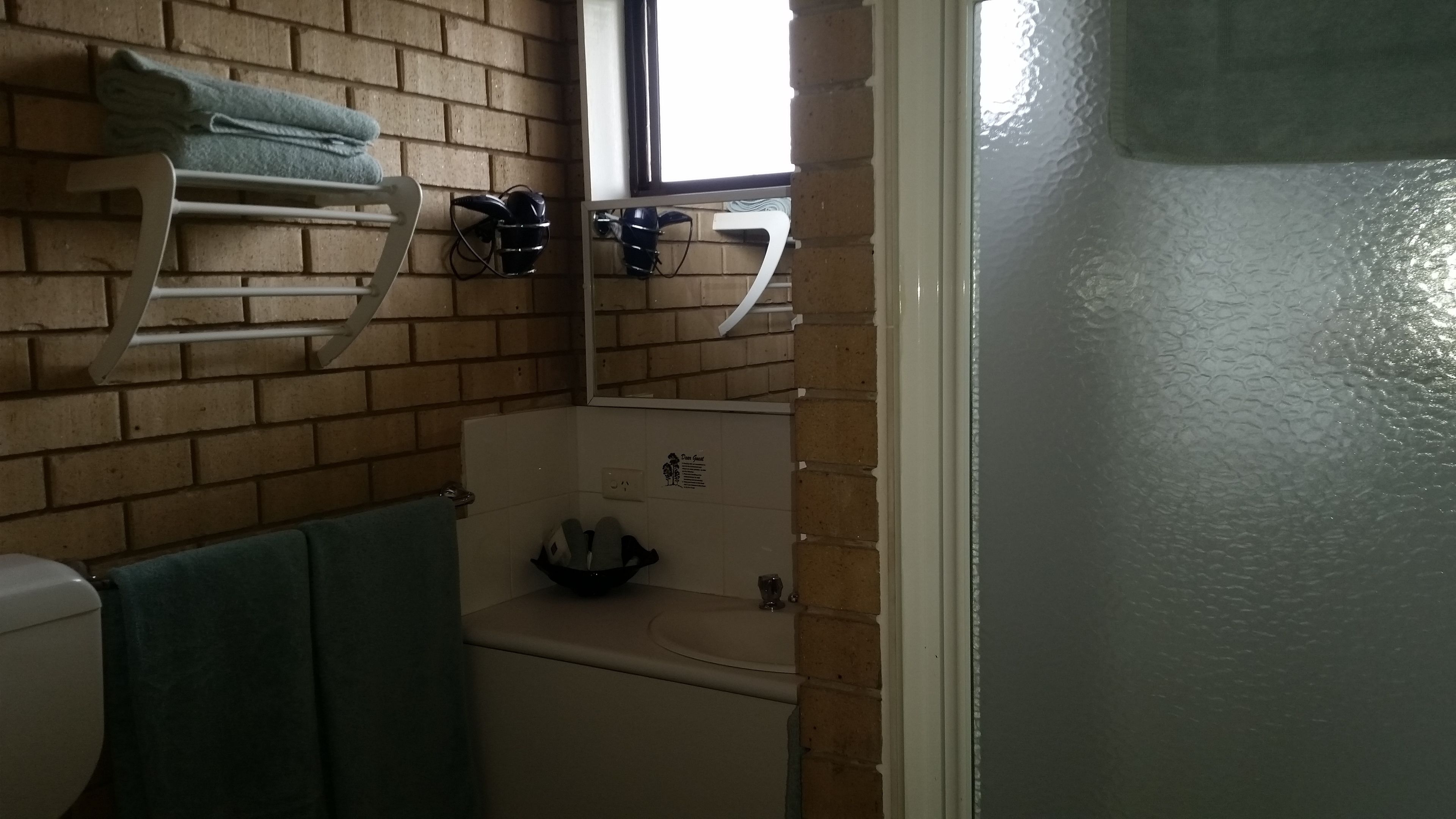 Casa de banho com parede de tijolos, lavatório branco e suporte para toalhas.