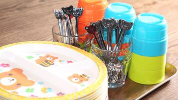 Uma bandeja com pratos empilhados, saleiros e pimenteiros coloridos, e um recipiente de vidro com utensílios.
