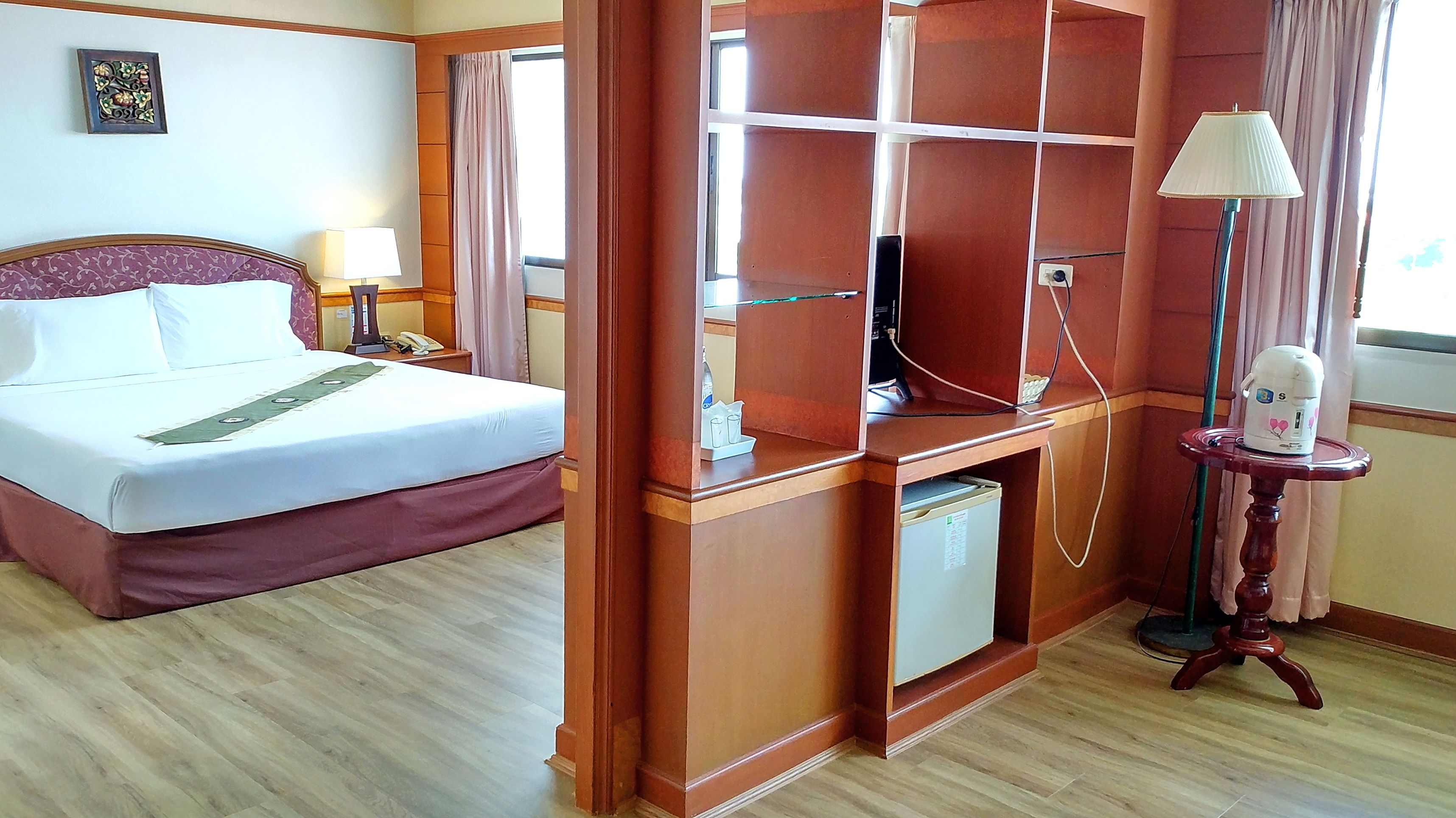 Quarto de hotel com cama, escrivaninha com luminária, máquina de café e pequeno frigorífico.