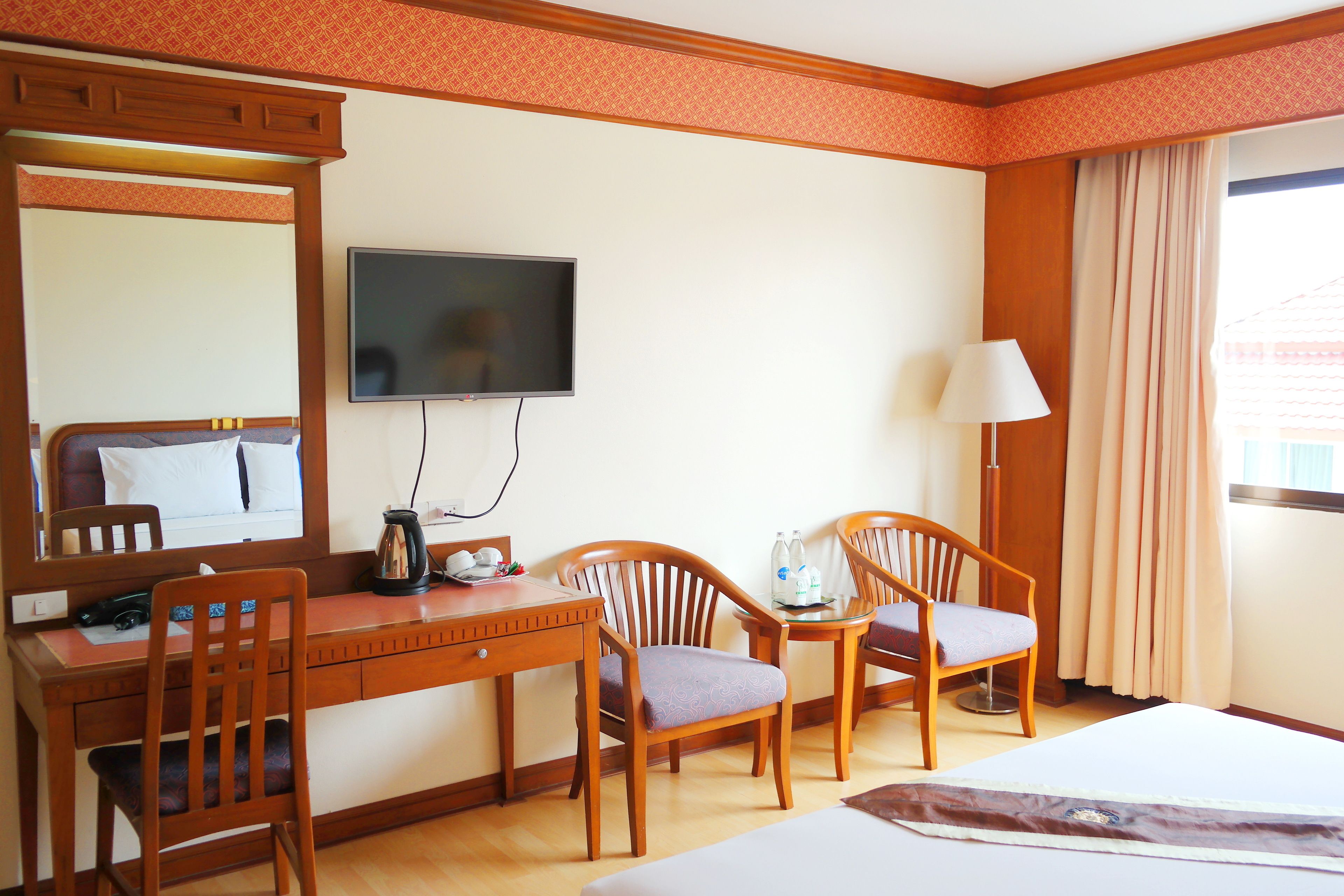 Quarto de hotel com escrivaninha de madeira, duas cadeiras, televisão, abajur e uma cama.