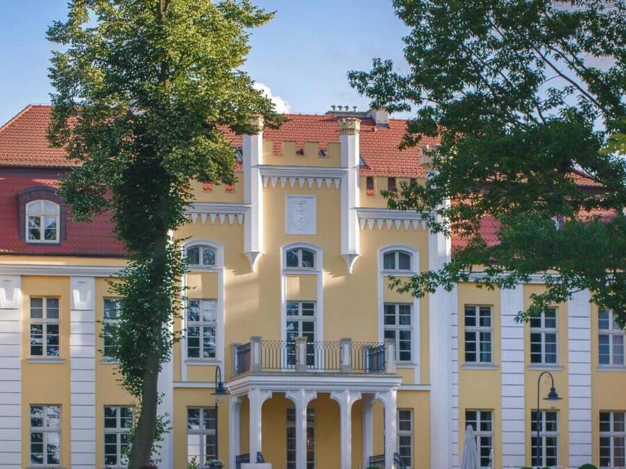 Um edifício histórico com telhado de telhas vermelhas, várias janelas e uma varanda central.