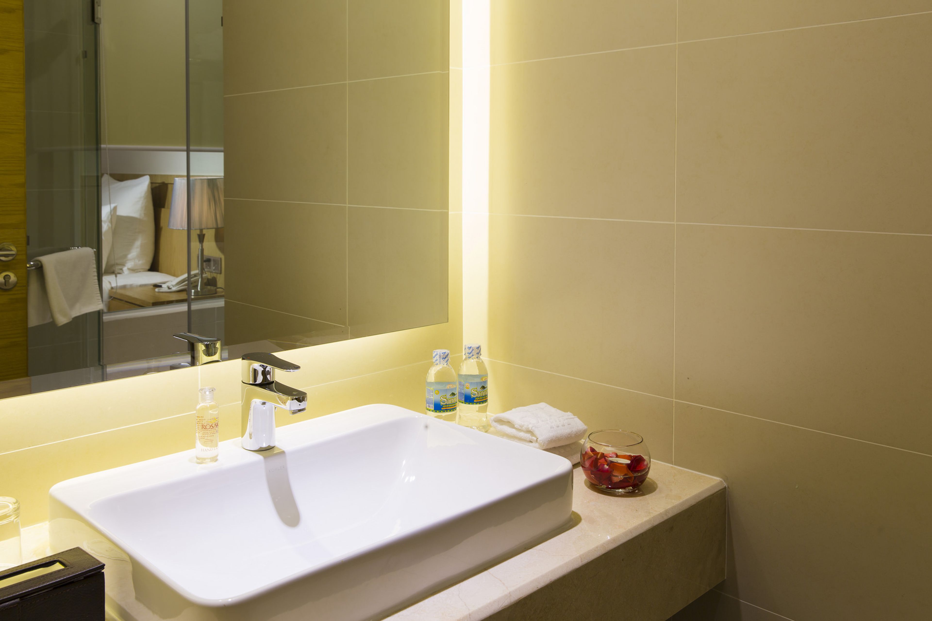 Um banheiro de hotel com uma pia grande branca, um espelho e duas embalagens de sabonete líquido.