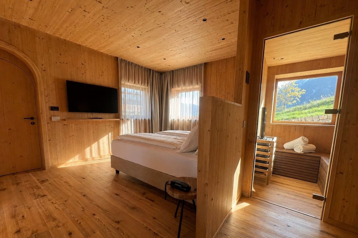 Quarto de madeira com uma cama, uma televisão e uma janela com vista para o verde.
