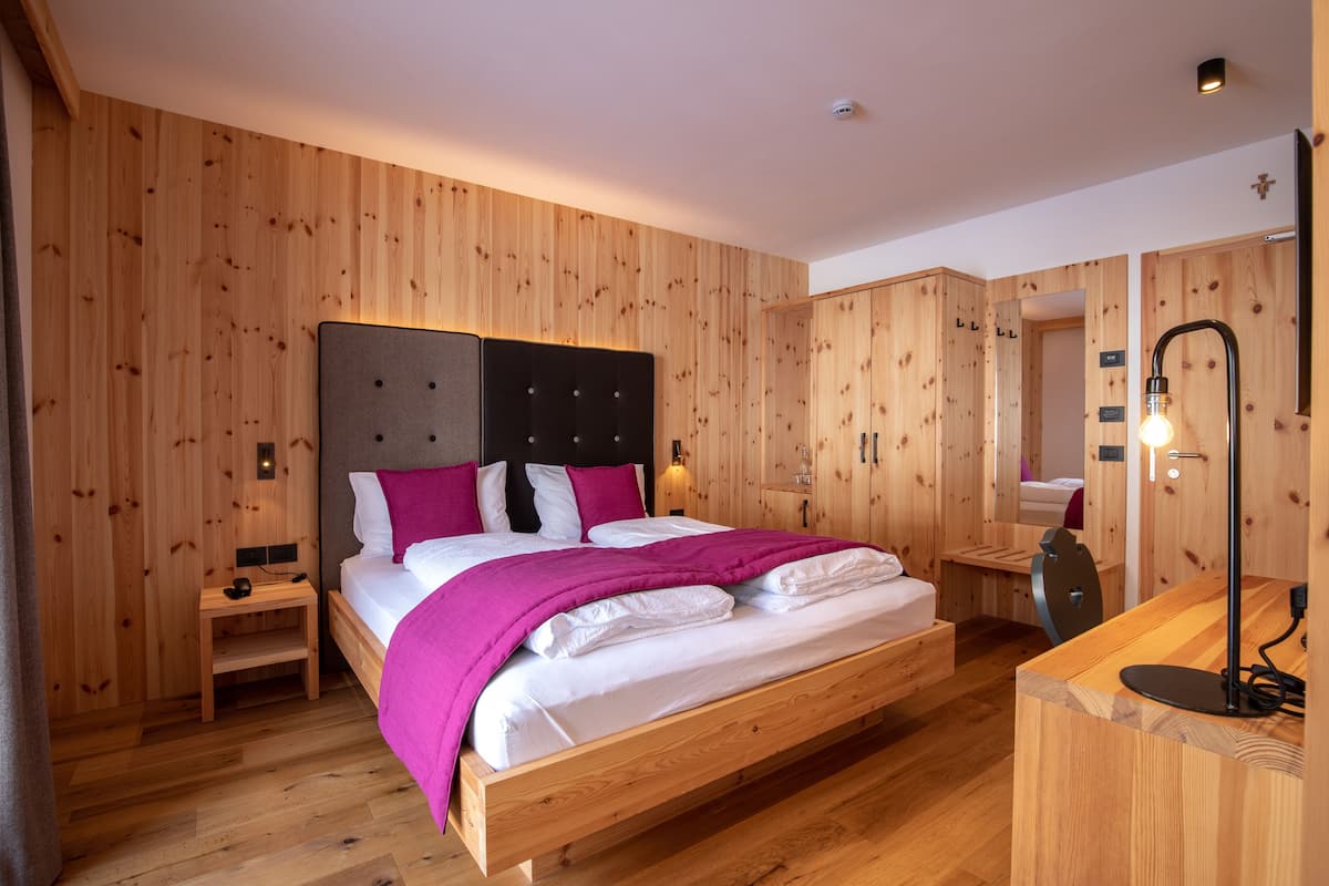 Quarto com painéis de madeira, uma cama, mesas de cabeceira, uma escrivaninha e um espelho.