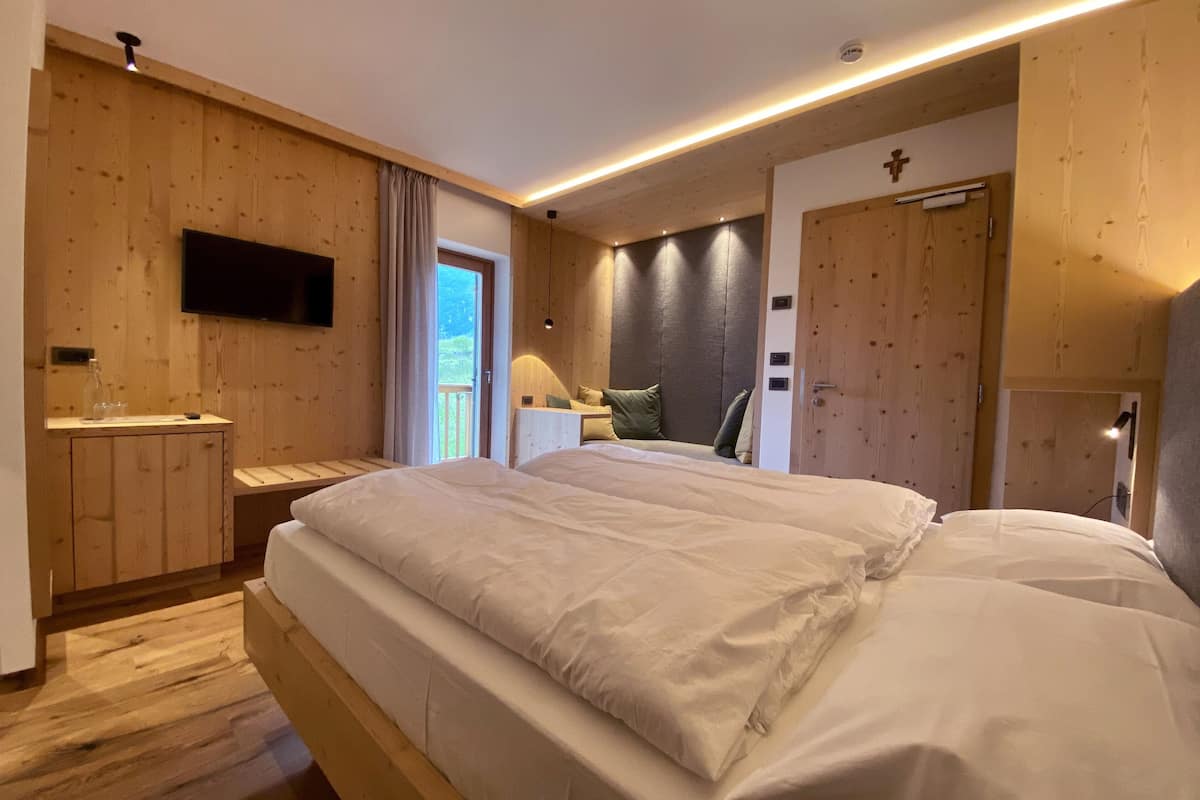 Quarto moderno com cama grande, paredes de madeira, TV montada e uma pequena mesa de cabeceira.