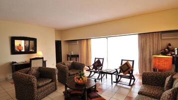 Sala de estar com sofás estampados, uma mesa de centro redonda com frutas e vista para o exterior através de grandes janelas.