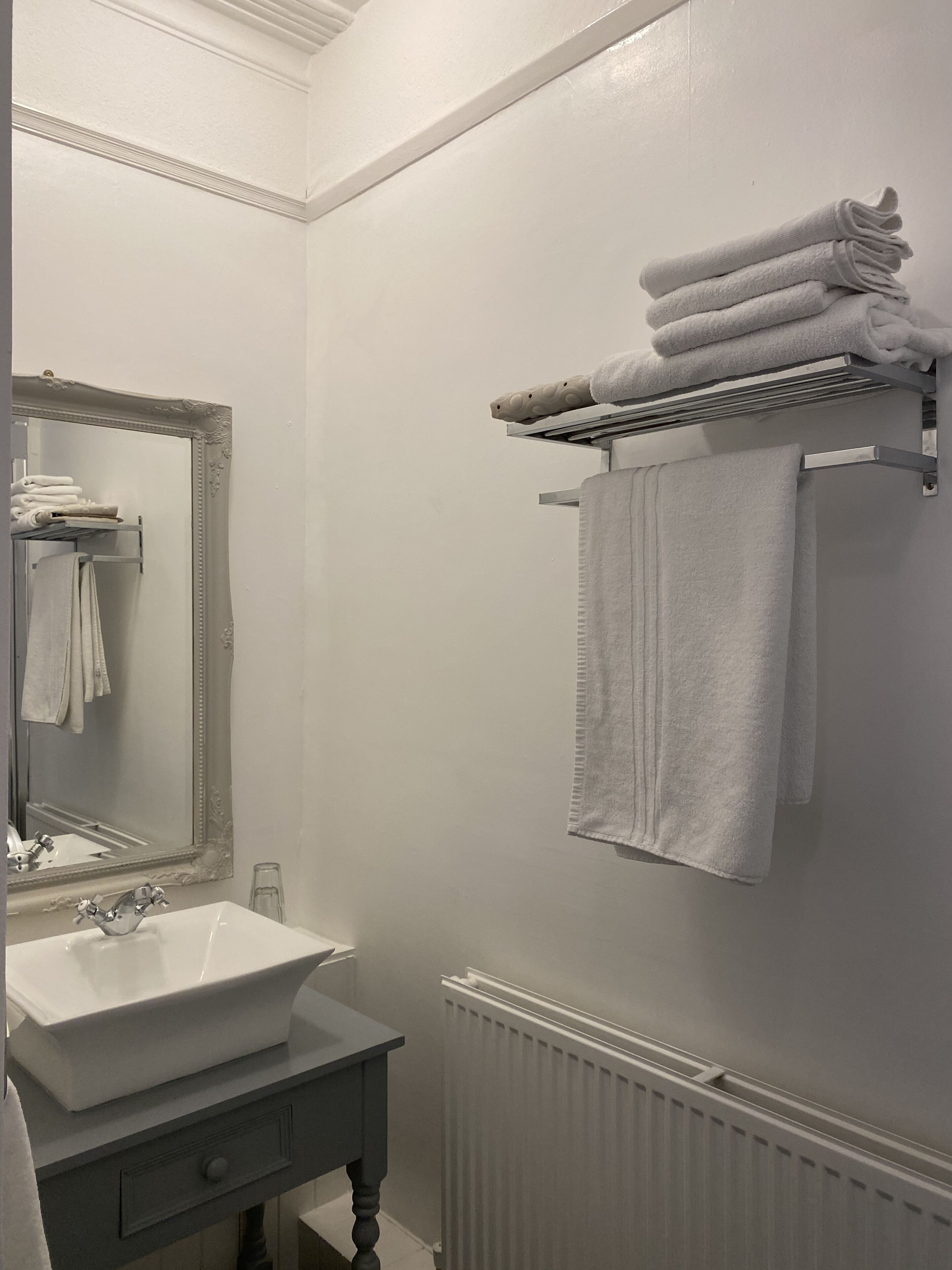 Casa de banho com lavatório branco, espelho, porta-toalhas e radiador.