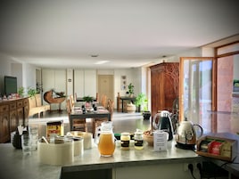 Uma área de refeições com uma mesa comprida, cadeiras e uma máquina de café. Há diversos recipientes e potes na bancada.