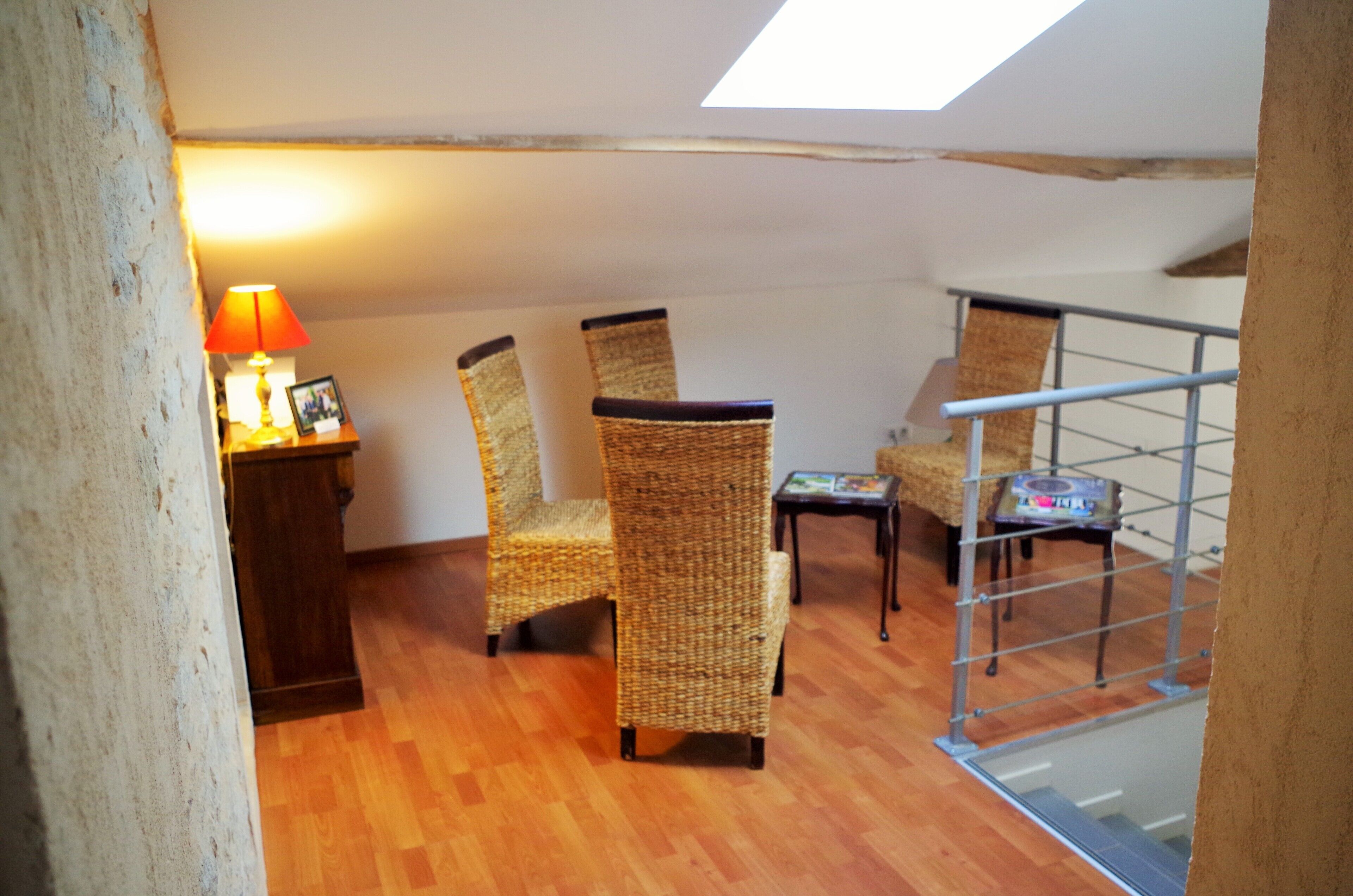 Quarto de loft aconchegante com claraboia, cadeiras de vime, uma mesinha e guarda-corpo de metal.