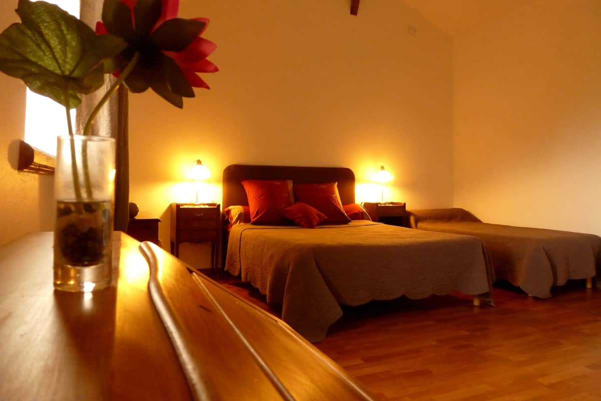 Quarto com duas camas, mesa de cabeceira com um vaso de flores e duas luminárias.
