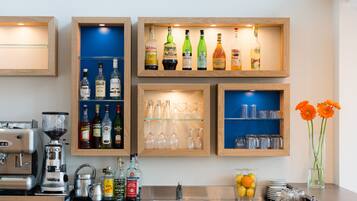 Uma área de bar com prateleiras de garrafas de bebidas, copos e uma máquina de café.