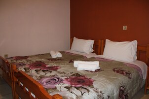 Cama bem arrumada com roupa de cama florida, cabeceira de madeira e interruptor de luz fixado na parede.