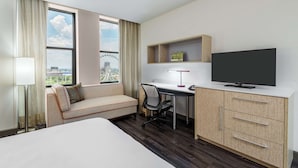 Quarto de hotel com uma cama, uma escrivaninha com cadeira, televisão, abajur e vista para uma roda gigante.