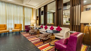 Um hall de hotel moderno com um sofá, poltronas, uma mesa de centro e um tapete estampado.