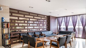 Uma área de estar moderna com assentos de couro, mesas de madeira e uma estante de livros.
