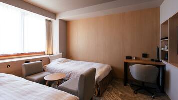 Quarto de hotel com duas camas, uma escrivaninha, uma cadeira, uma mesa redonda pequena e uma janela grande com cortinas.