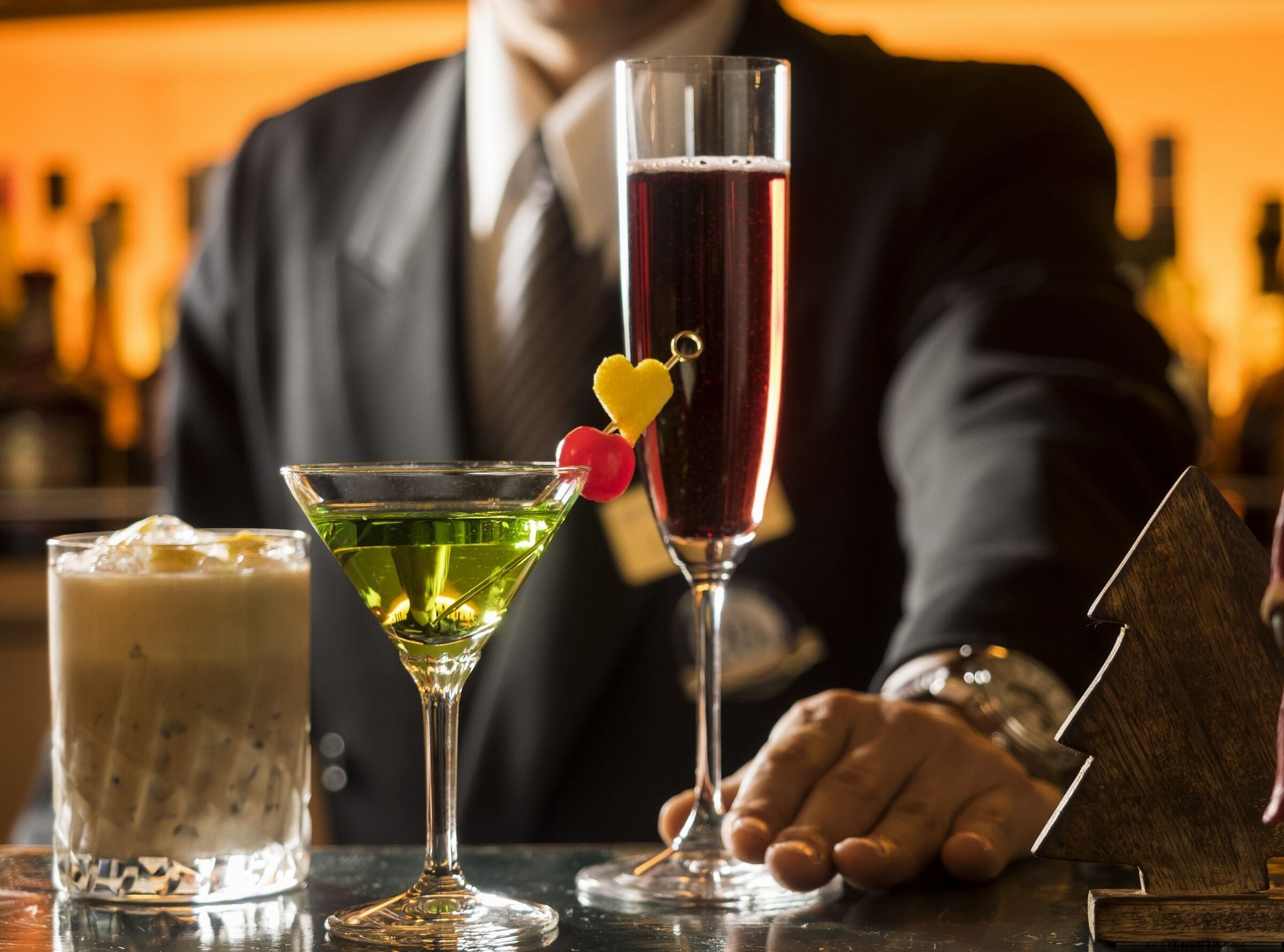 Um bar com três bebidas, um barman e um balcão de madeira.