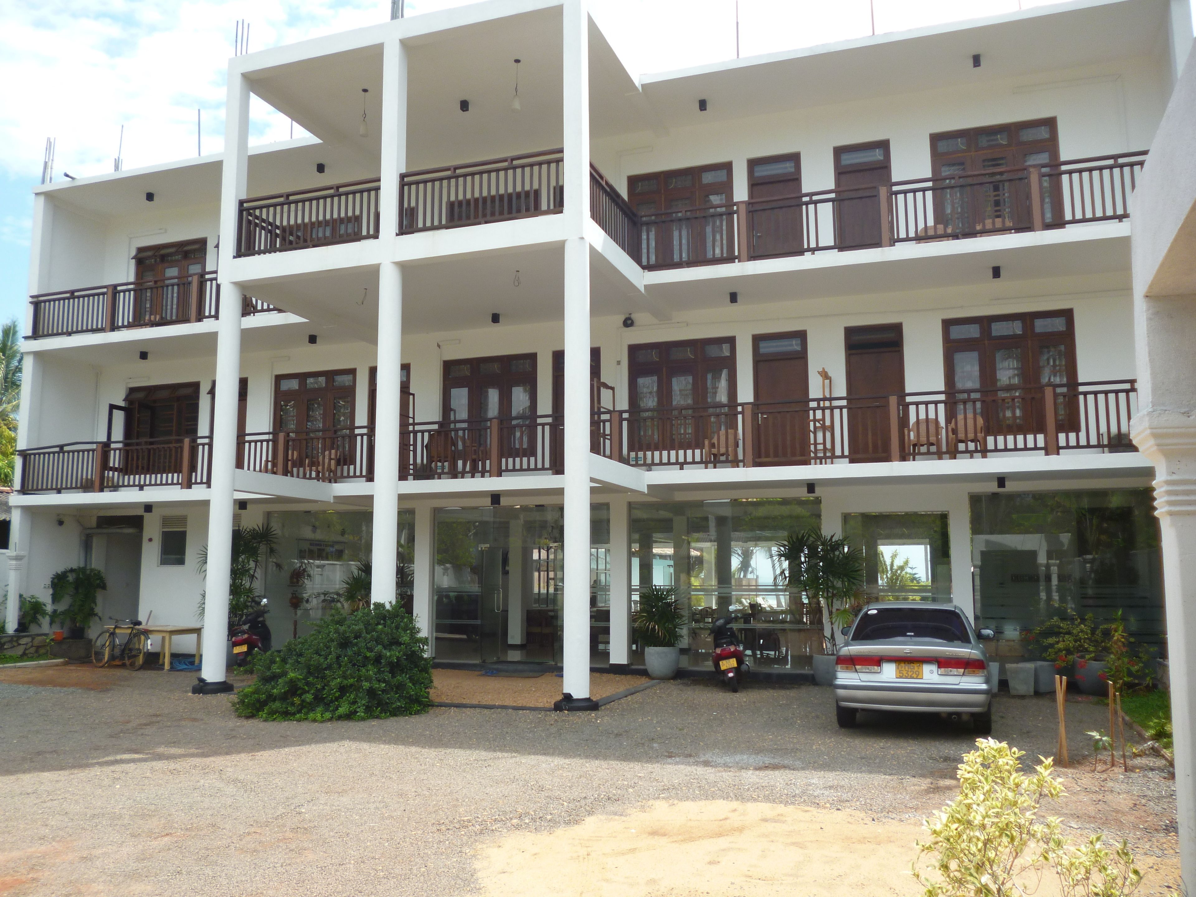 Um hotel de vários andares com varandas, entrada coberta e acesso por caminho de cascalho.