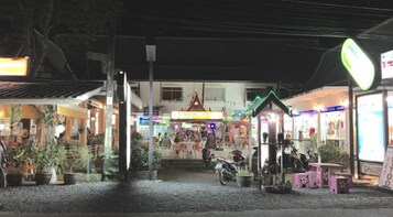 Cena noturna de uma rua com lojas e um edifício com telhado tradicional.