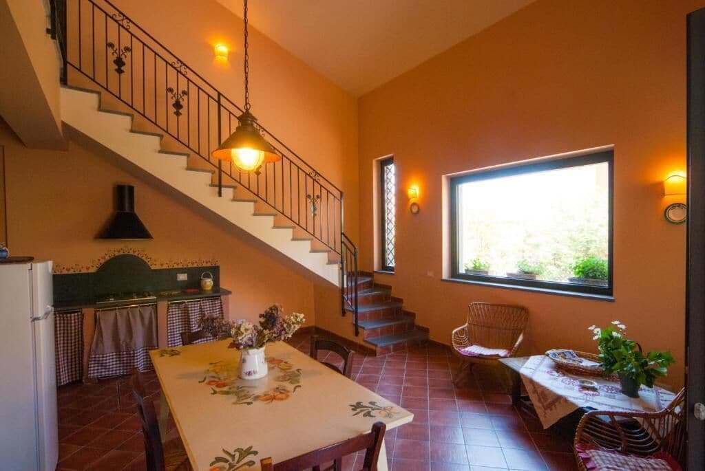 Uma sala de jantar com escada, uma mesa com um vaso de flores e uma janela com vista.