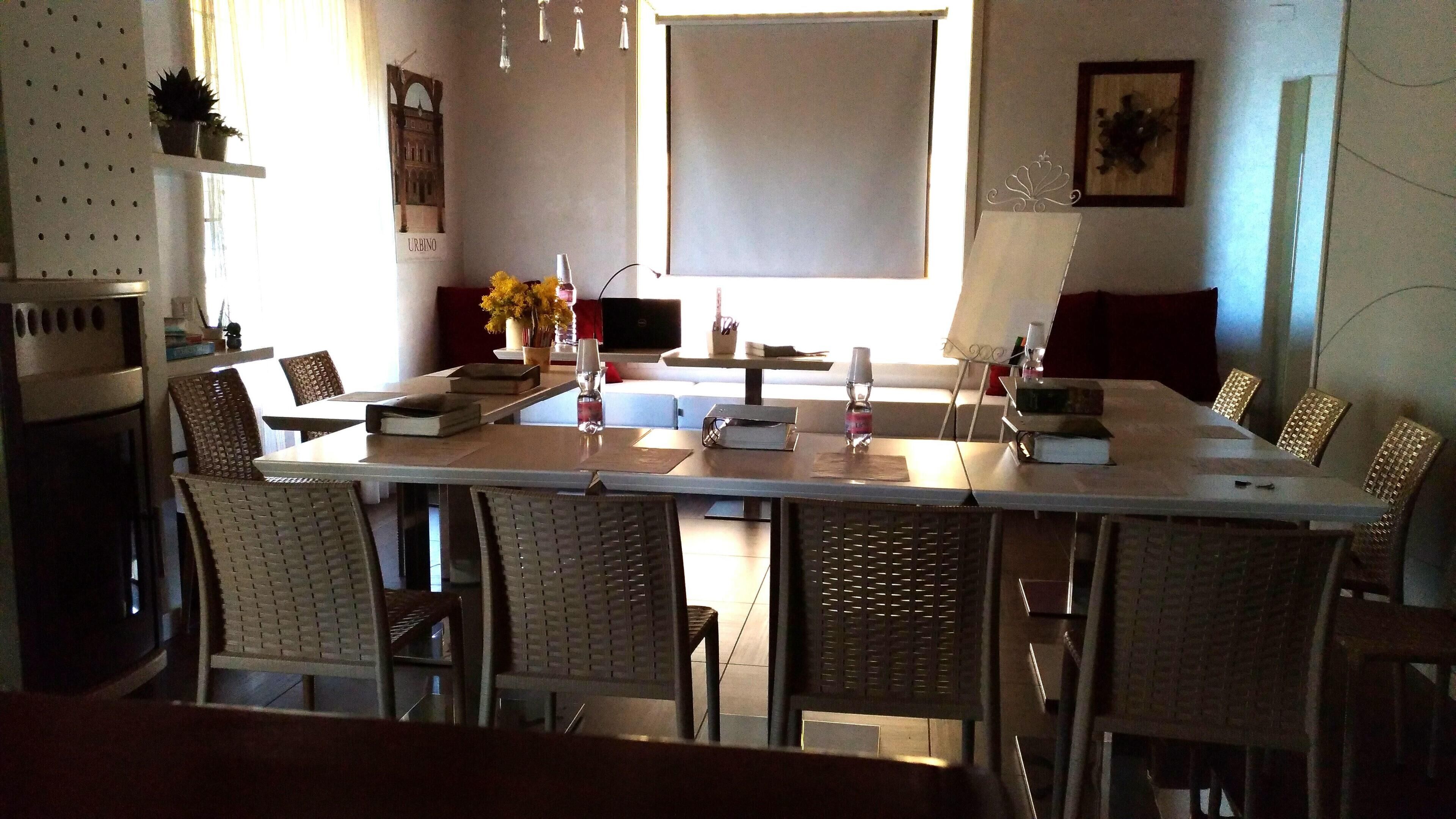 Uma área de refeições com uma mesa comprida, cadeiras de vime e um quadro branco.
