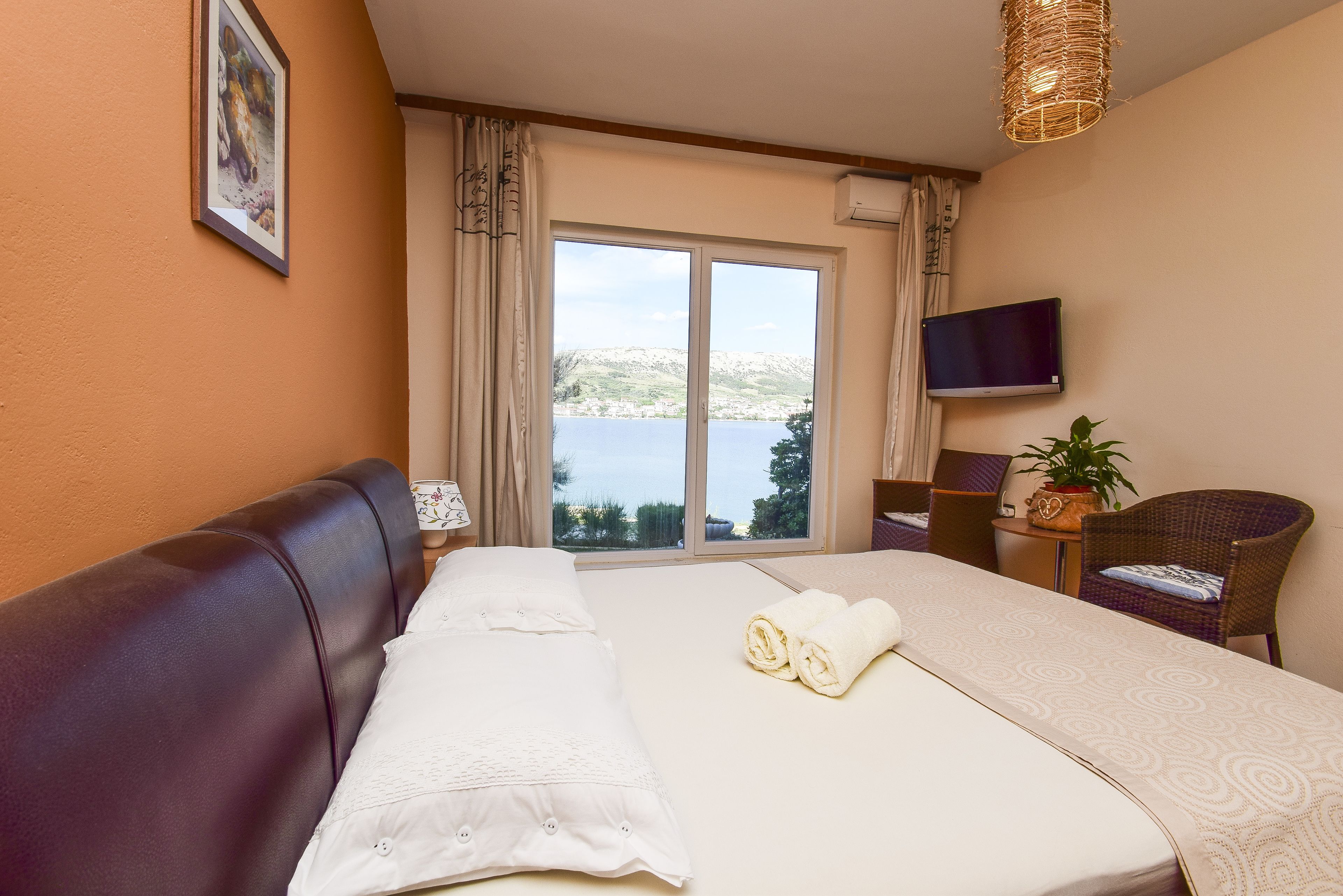 Quarto de hotel com cama, sofá, televisão, poltrona e vista para o mar.