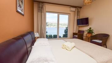 Quarto de hotel com cama, sofá, televisão, poltrona e vista para o mar.