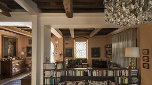 Uma biblioteca acolhedora com estantes, um espaço de leitura confortável e um lustre clássico.