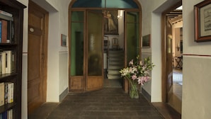 Um corredor com porta de madeira, escada e um vaso de flores.