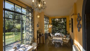 Uma sala de jantar com grandes janelas, um candelabro e uma mesa posta para refeição.