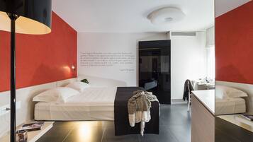 Quarto de hotel moderno com uma cama grande, mesa de cabeceira e um espaço para leitura.