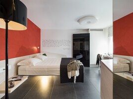 Quarto de hotel moderno com uma cama grande, mesa de cabeceira e um espaço para leitura.