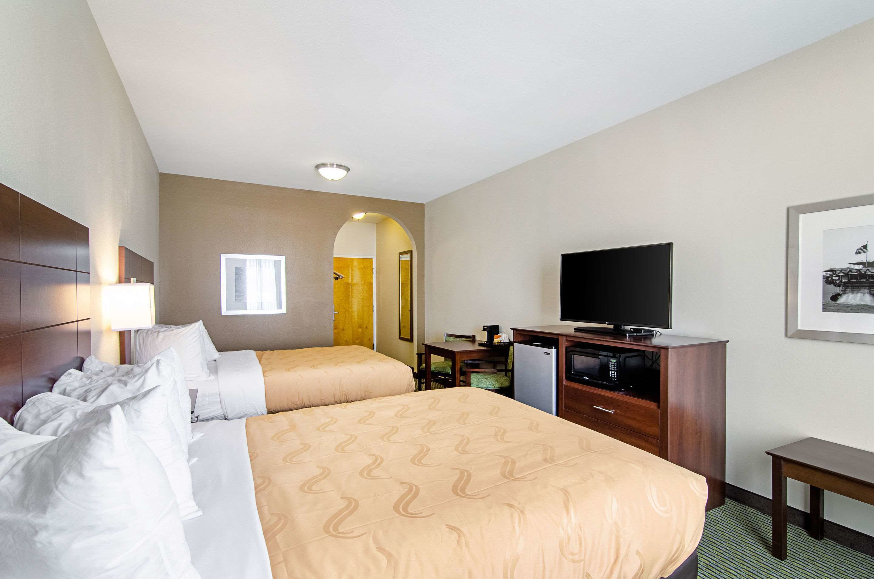 Quarto de hotel com duas camas, uma televisão, uma escrivaninha e uma mesa pequena.