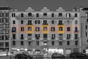 Um edifício com várias andares, varandas, um café e uma entrada visível.