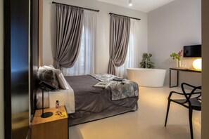 Quarto moderno com cama, mesa de cabeceira, cadeira, escrivaninha, televisão e banheiro.