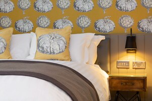 Cama bem arrumada com travesseiros brancos e amarelos, um cobertor marrom e uma mesa de cabeceira de madeira com abajur.