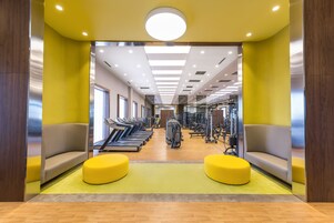 Academia com equipamentos de ginástica, esteiras e carpete amarelo.