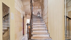 Uma escadaria com degraus de pedra e corrimão de metal, que leva a um quarto com janela e porta.